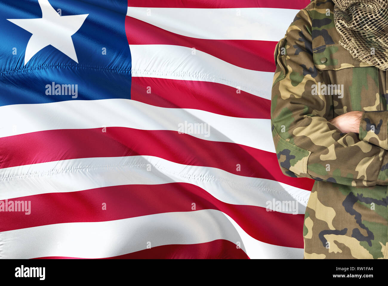 Crossed arms Liberian soldier with national waving flag on background ...