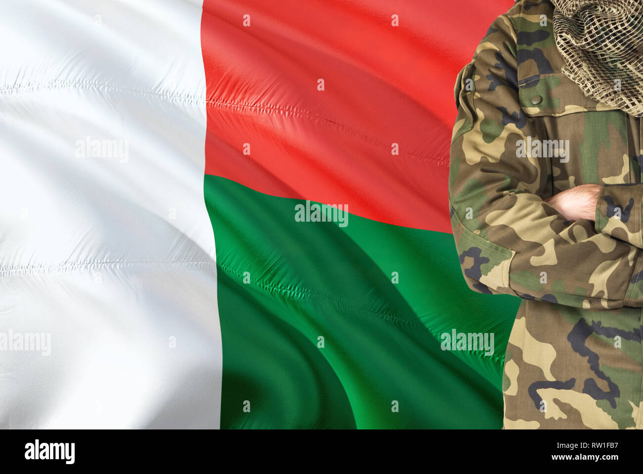 Crossed arms Malagasy soldier with national waving flag on background ...