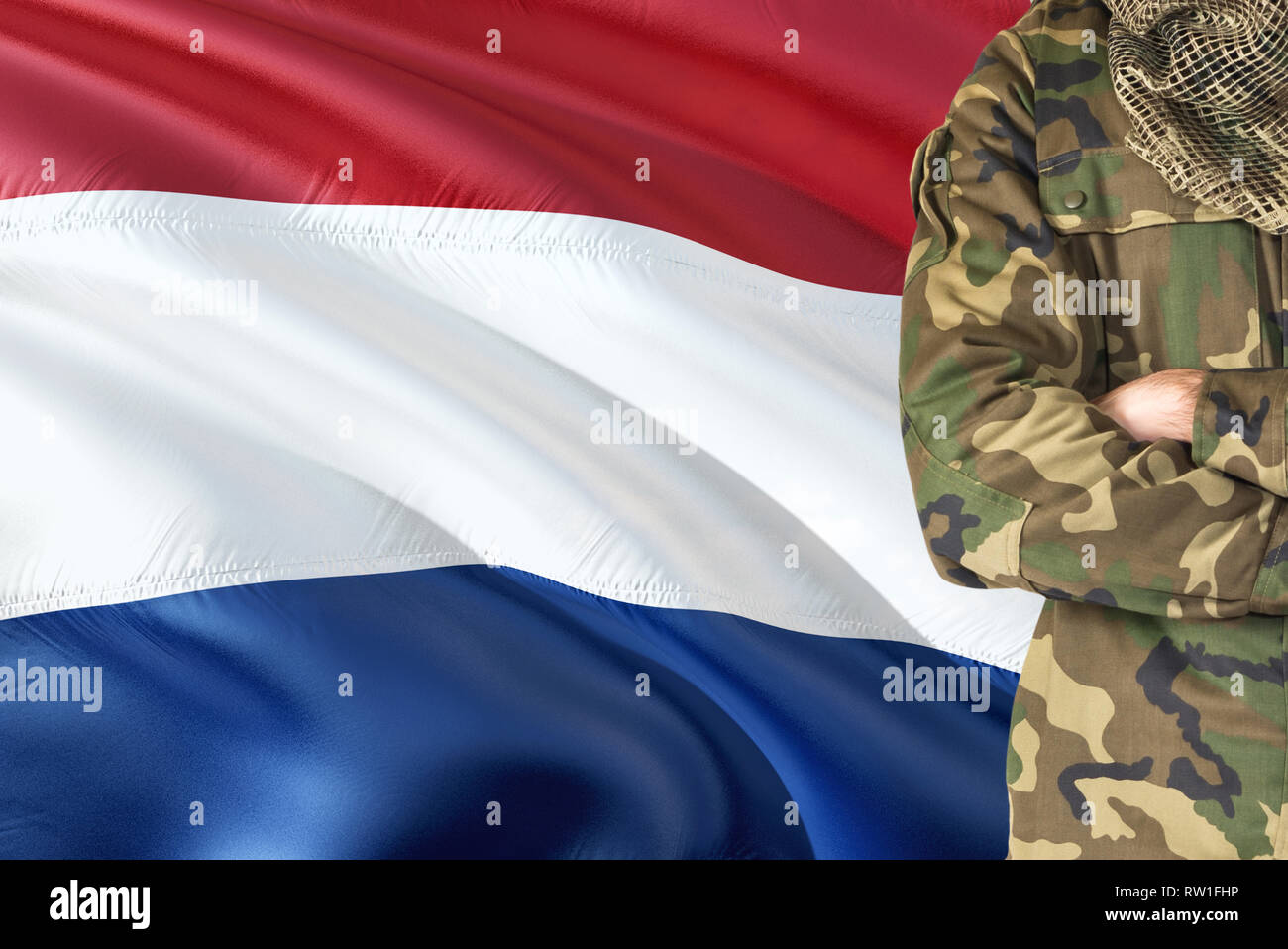 Crossed arms Dutch soldier with national waving flag on background ...