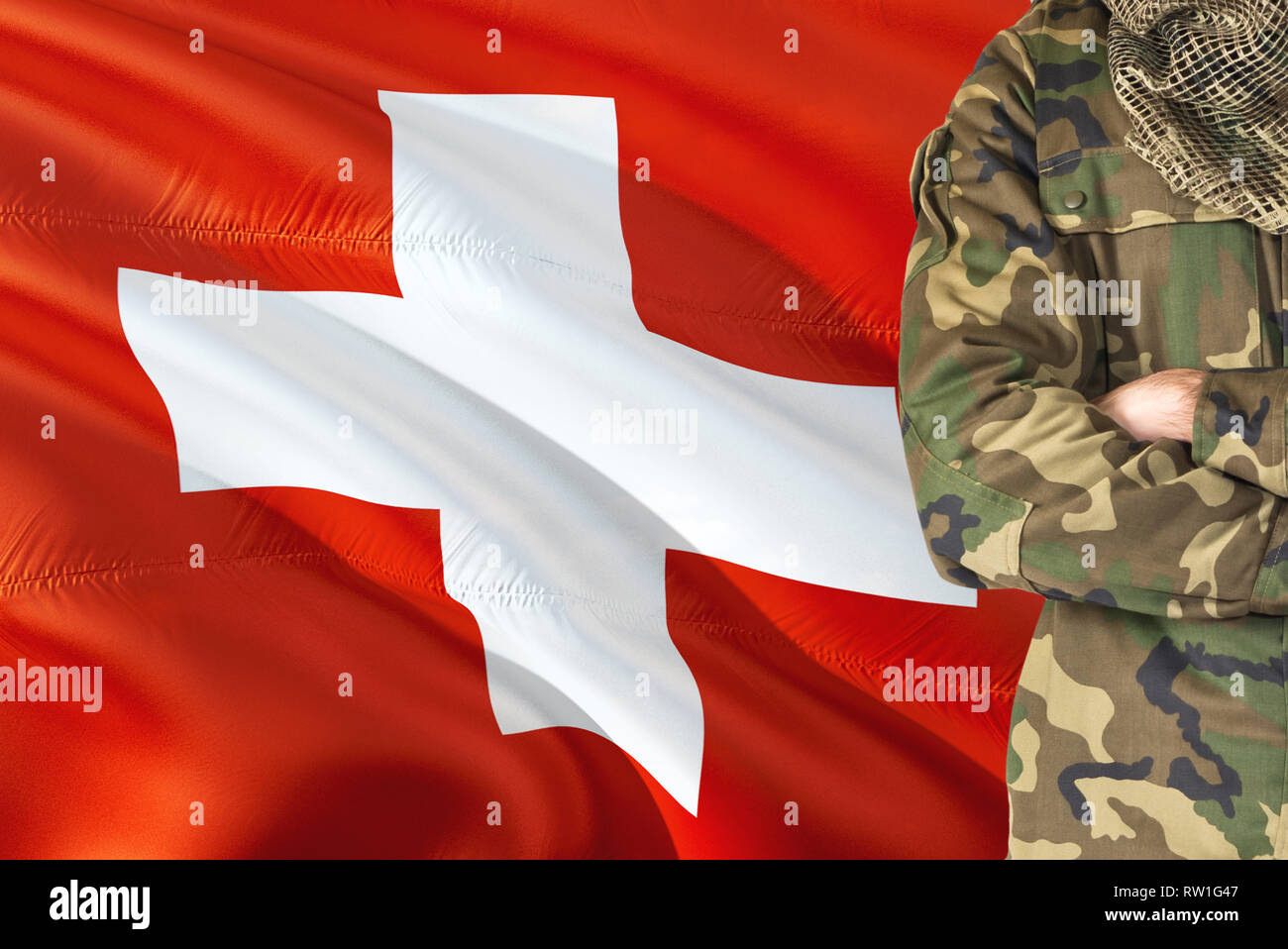 Crossed arms Swiss soldier with national waving flag on background ...