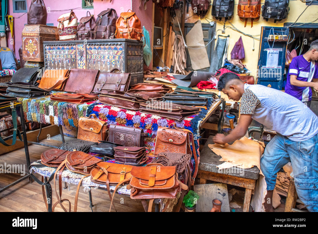 Merchant smooths out leather hide at market stall selling an assortment ...