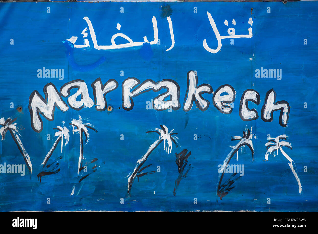 Blue and white hand-painted sign with Arabic and English spelling of ...