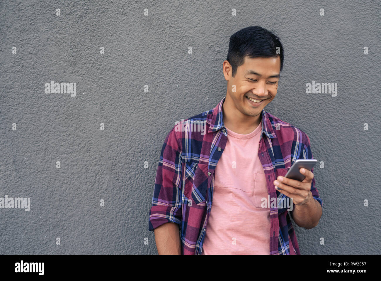 Smiling young Asian man reading a text on his cellphone Stock Photo - Alamy