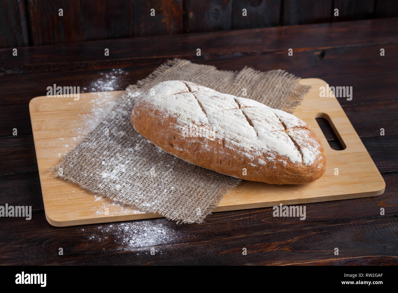 Fresh brown bread on an oak board with scattered flour on a wooden ...