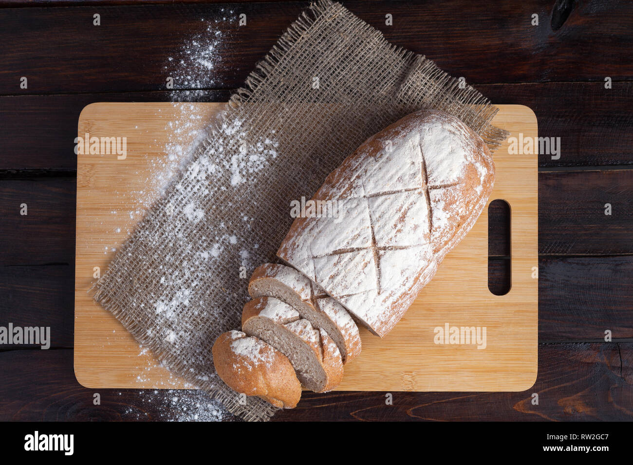 Fresh brown bread with sliced pieces on an oak board with scattered ...