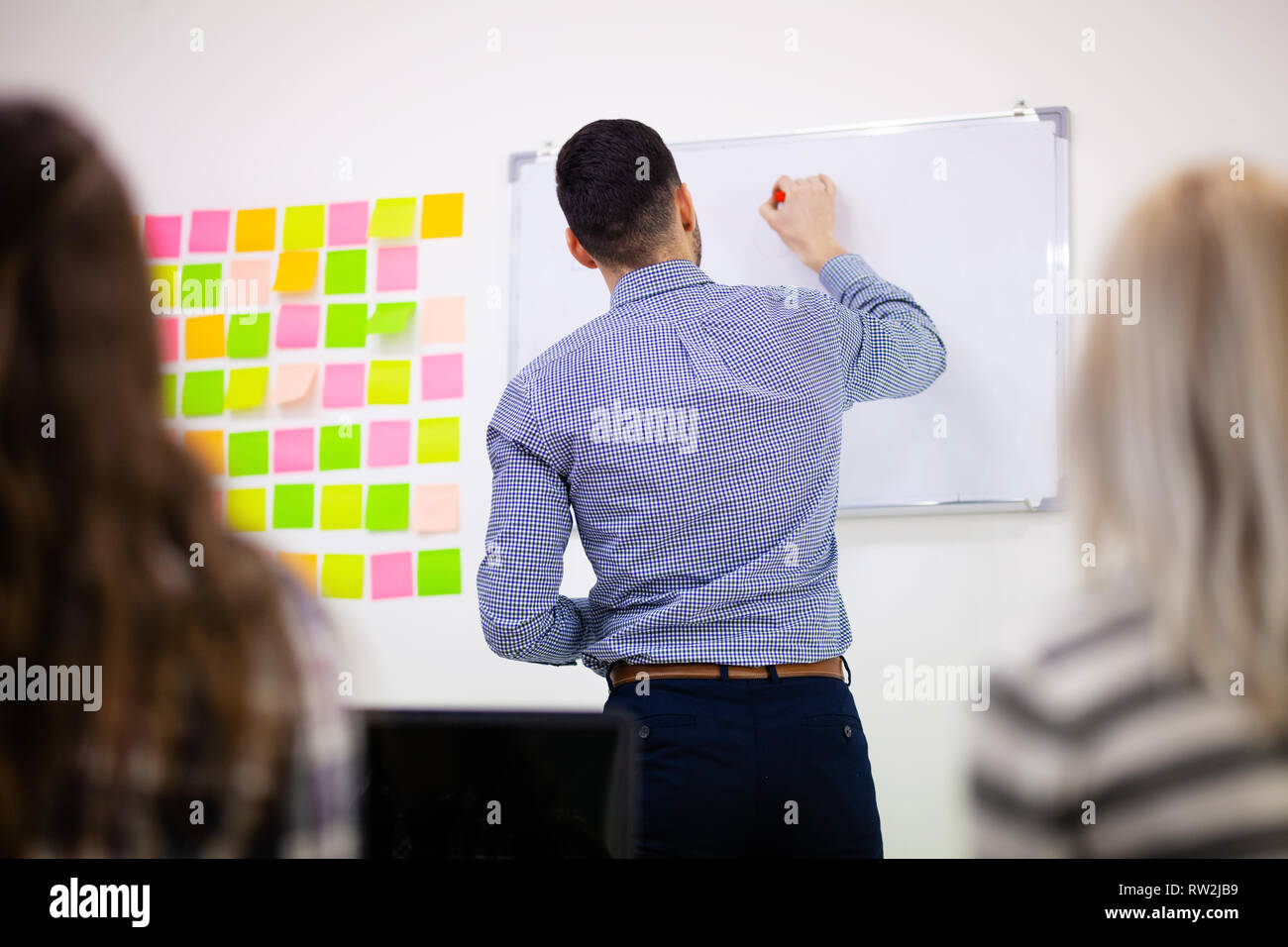 back view of a professor writing on a table in classroom with students ...