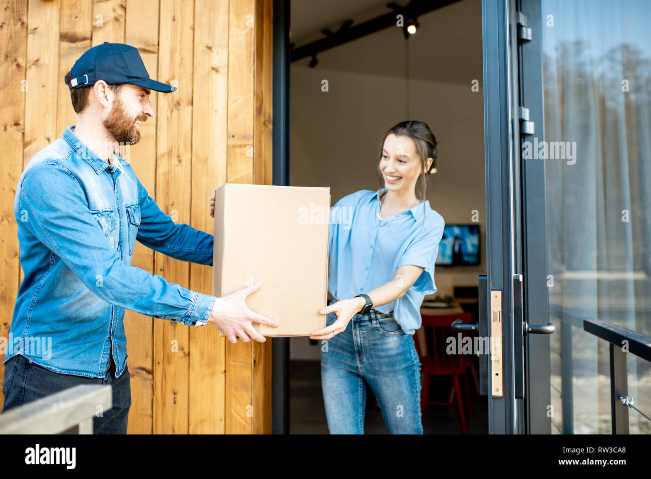 Delivery man bringing packaged goods to a young woman client standing ...