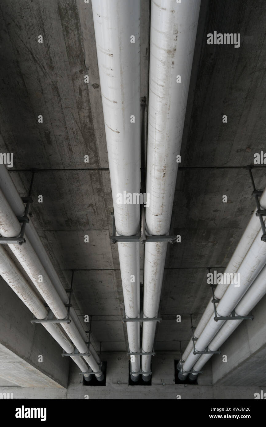 white industrial sewage and water pipes underneath a concrete bridge in ...