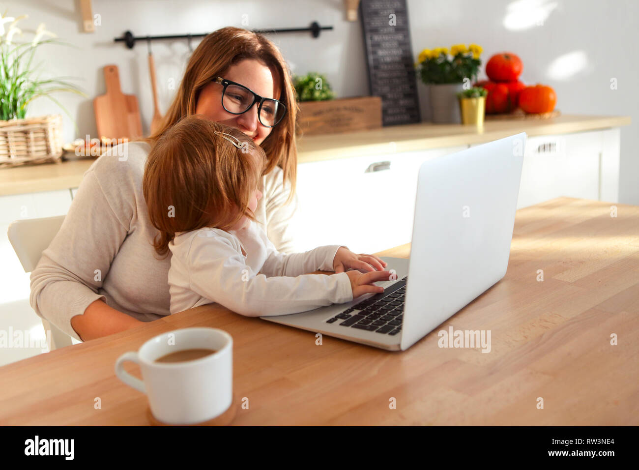 Beautiful smiling mom working at home on a laptop computer while taking ...