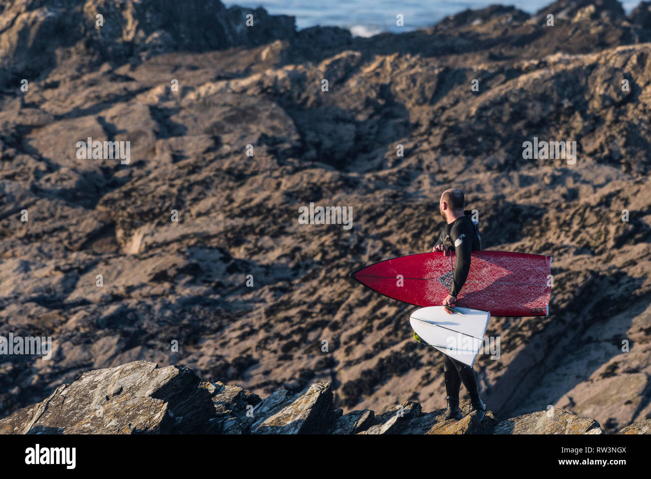 A surfer standing on rocks carrying his snapped surfboard at North ...