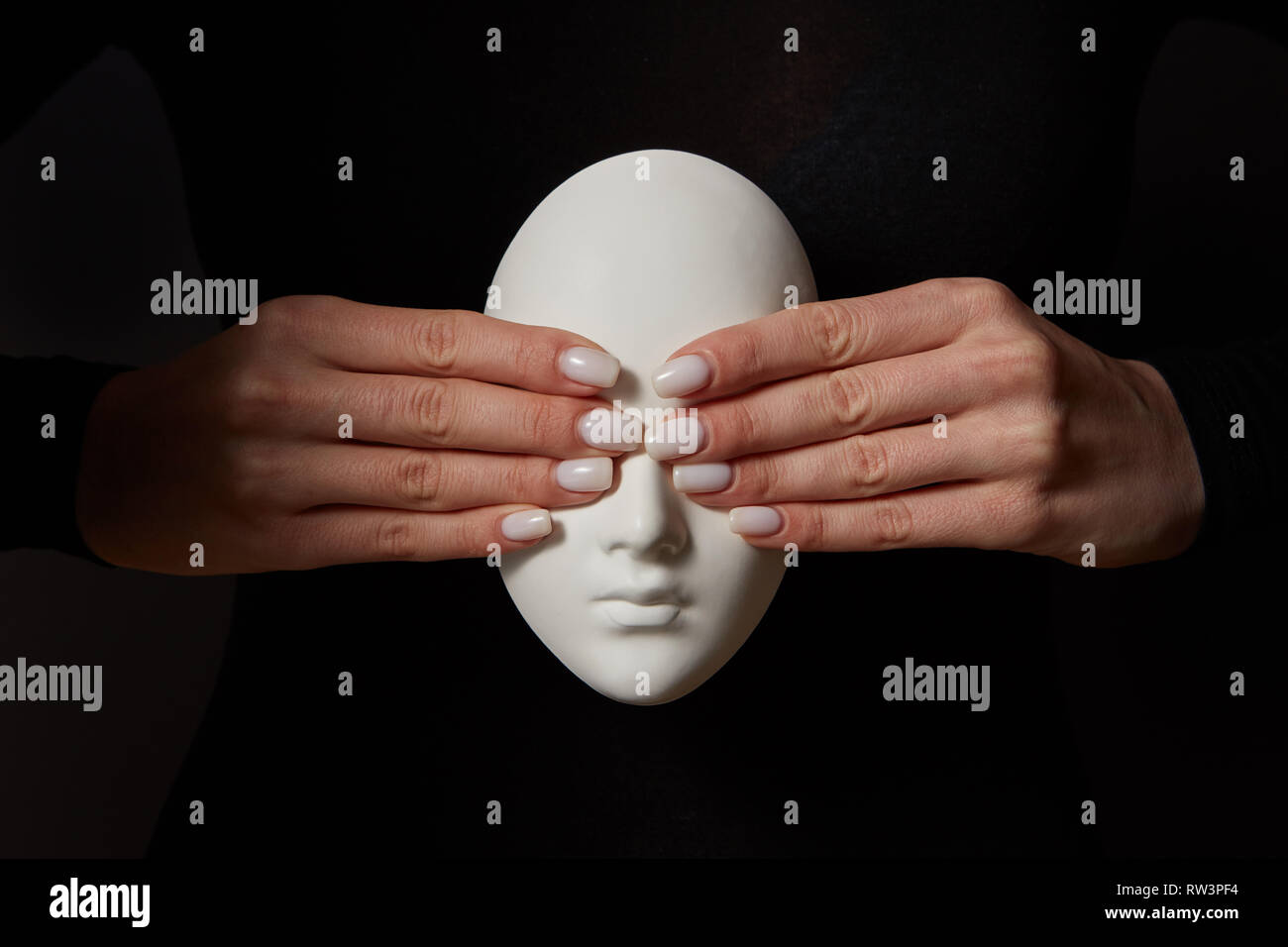 Woman's fingers close eyes of gypsum mask face on a black background ...