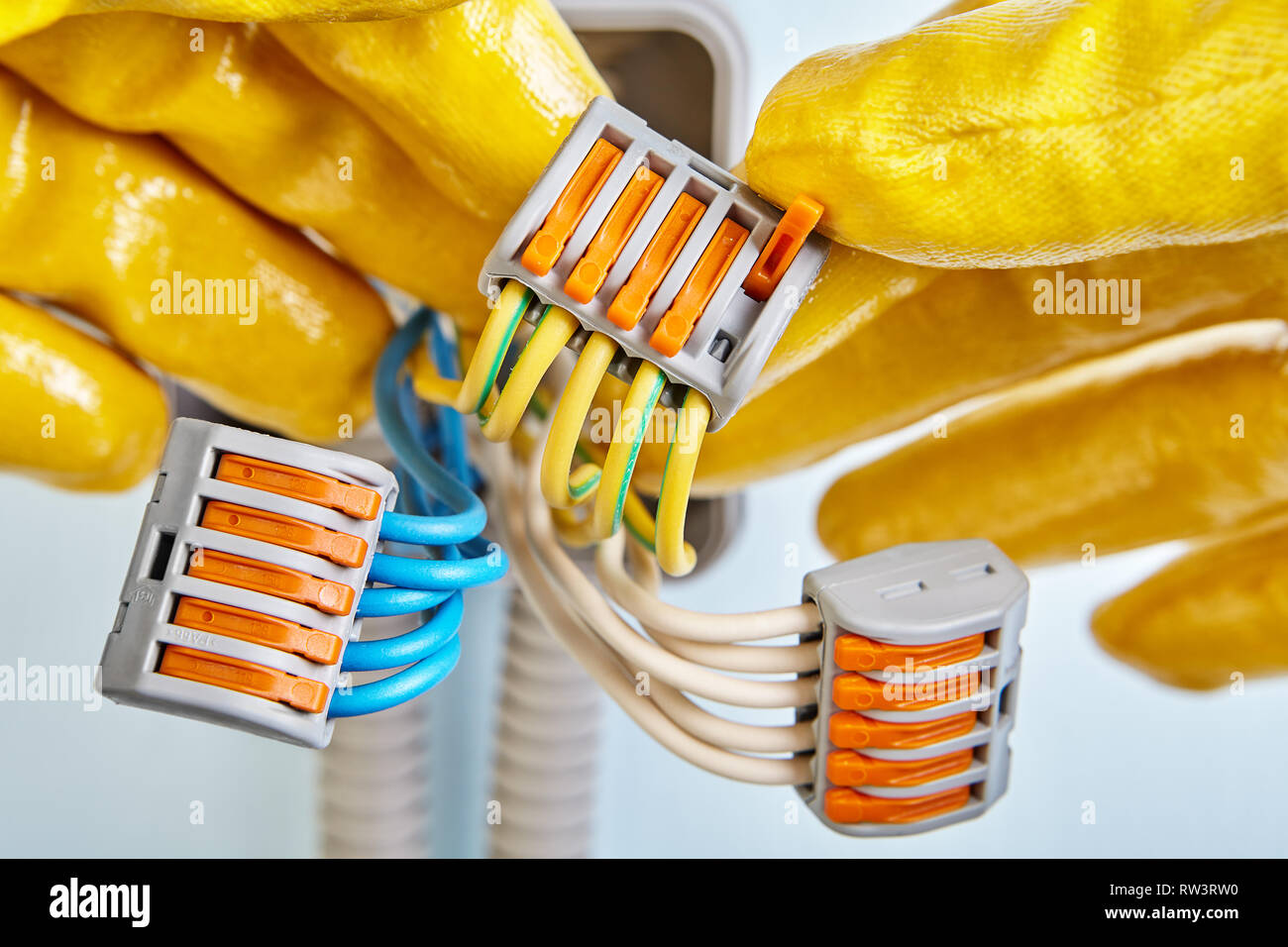 Electrician in yellow ptotective gloves holds electrical wires spliced ...