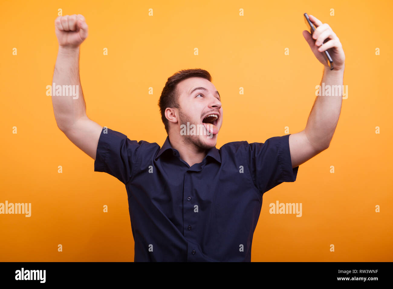 Excited young man raising up his arms on yellow background Stock Photo ...