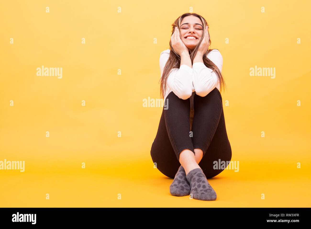 Silly woman making funny faces while sitting down on yellow background ...