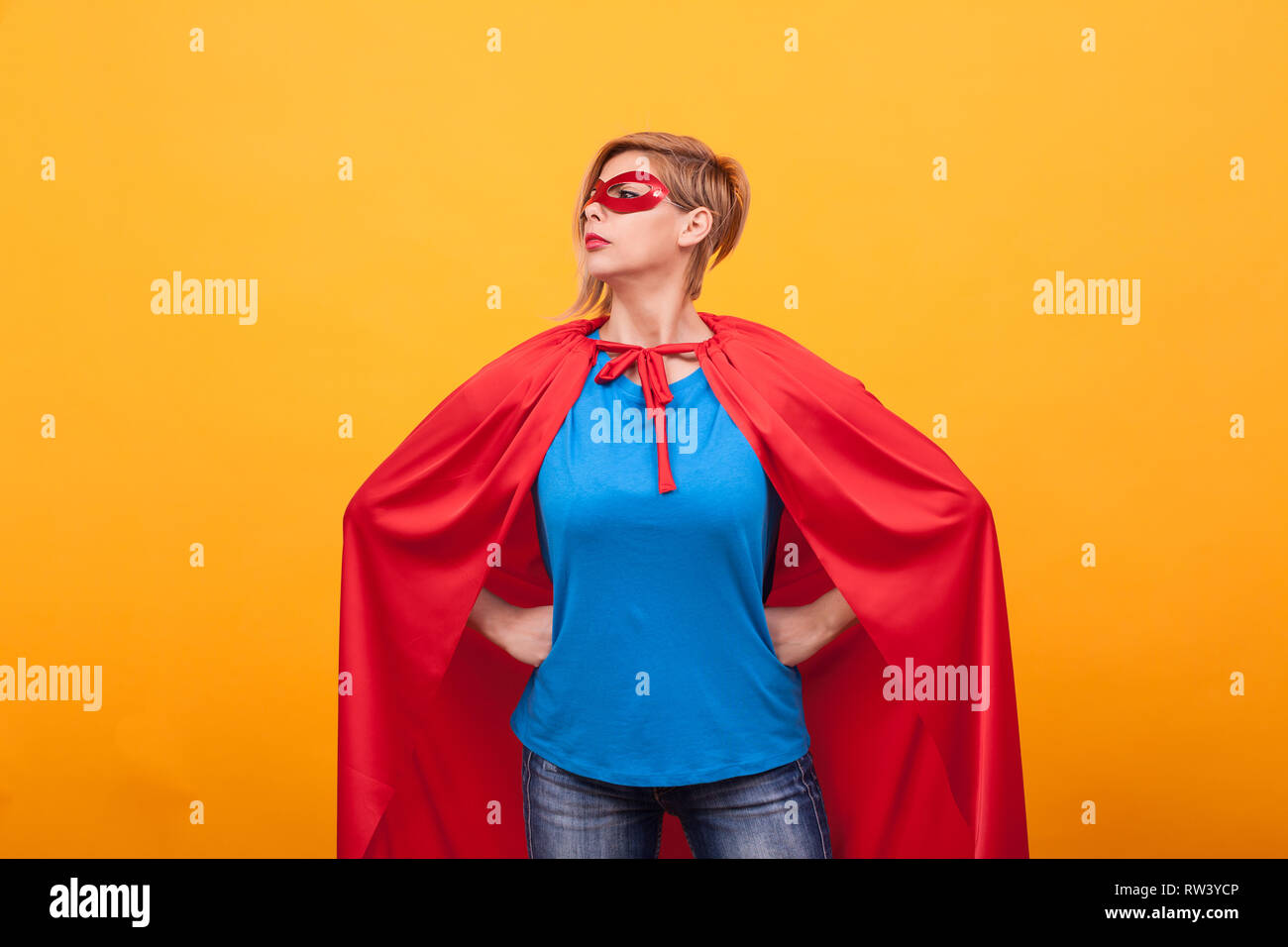 Young woman in superheros costume standing proudly over yellow ...