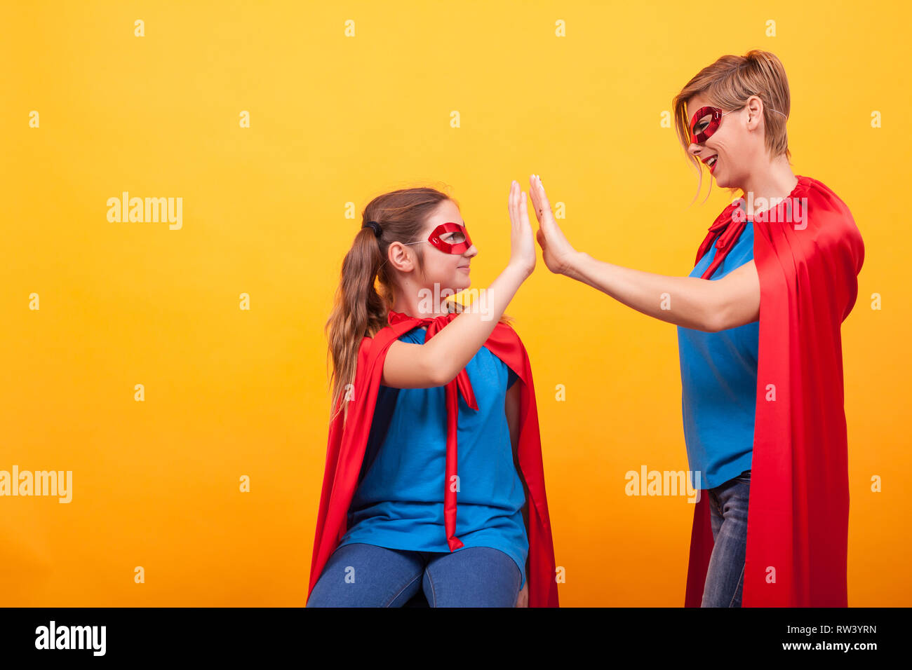 Mother and daughter dressed like superheros giving hi5 over yellow ...