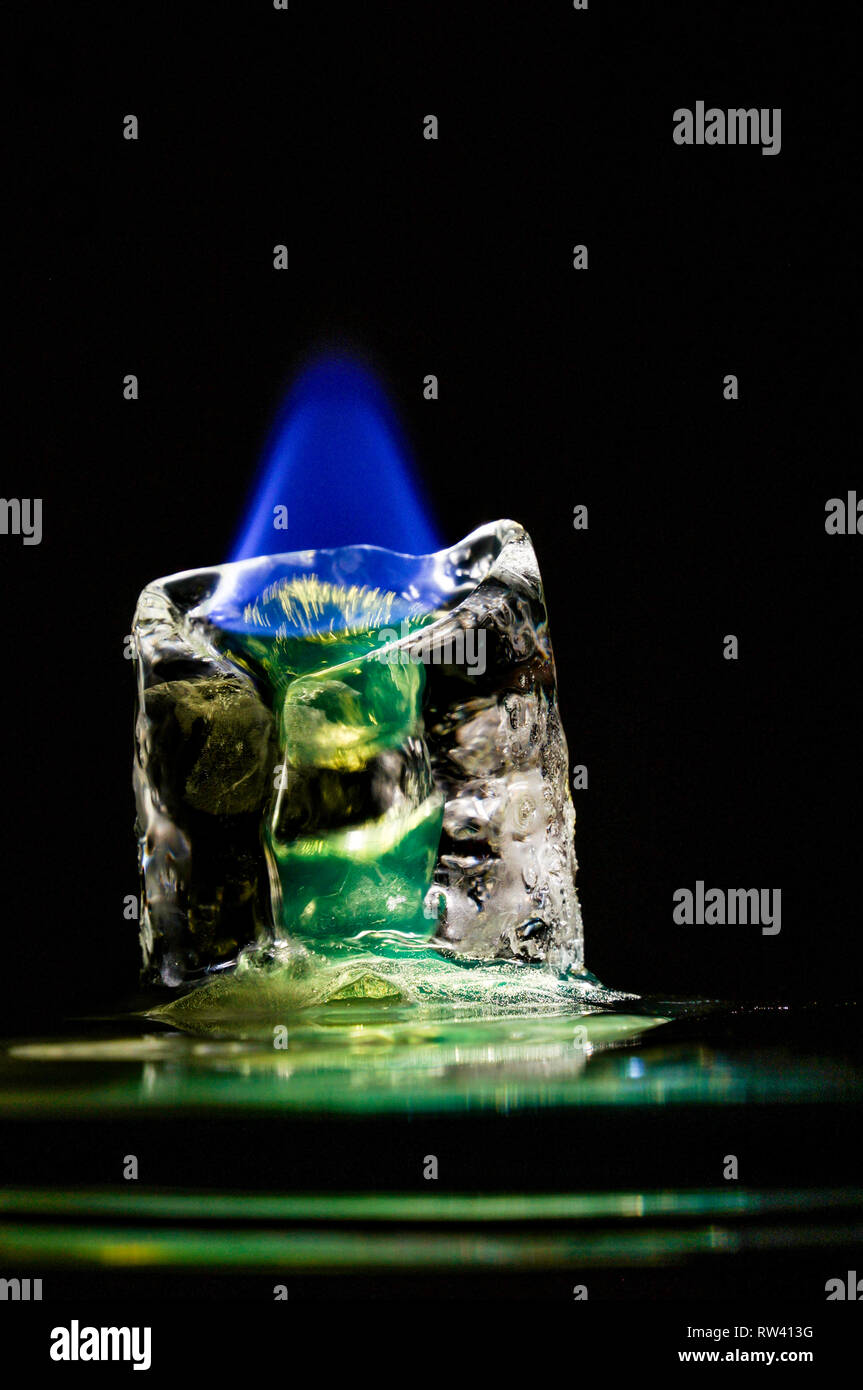Blue flame melting down greenish icecube in front of black background ...