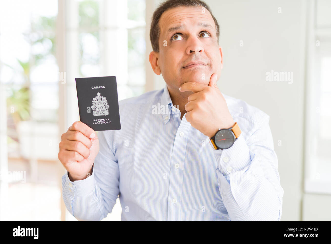 Middle age man holding holding Canadian passport serious face thinking ...