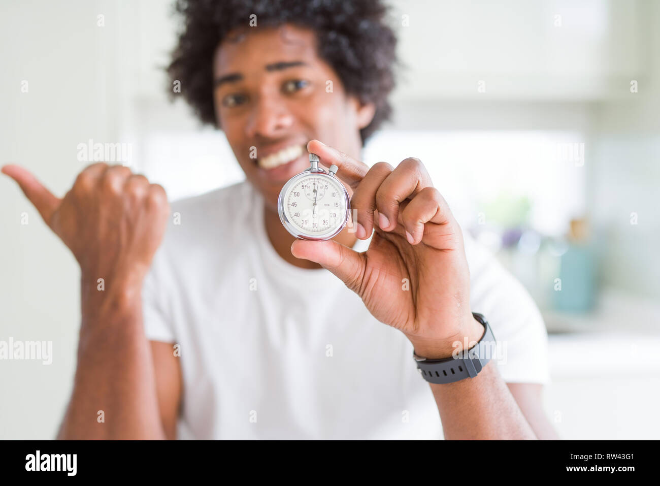 African American man holding stopwatch pointing and showing with thumb ...