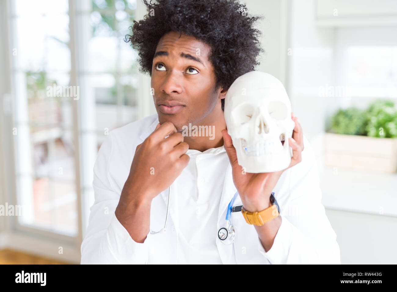 African American doctor man holding skull serious face thinking about ...