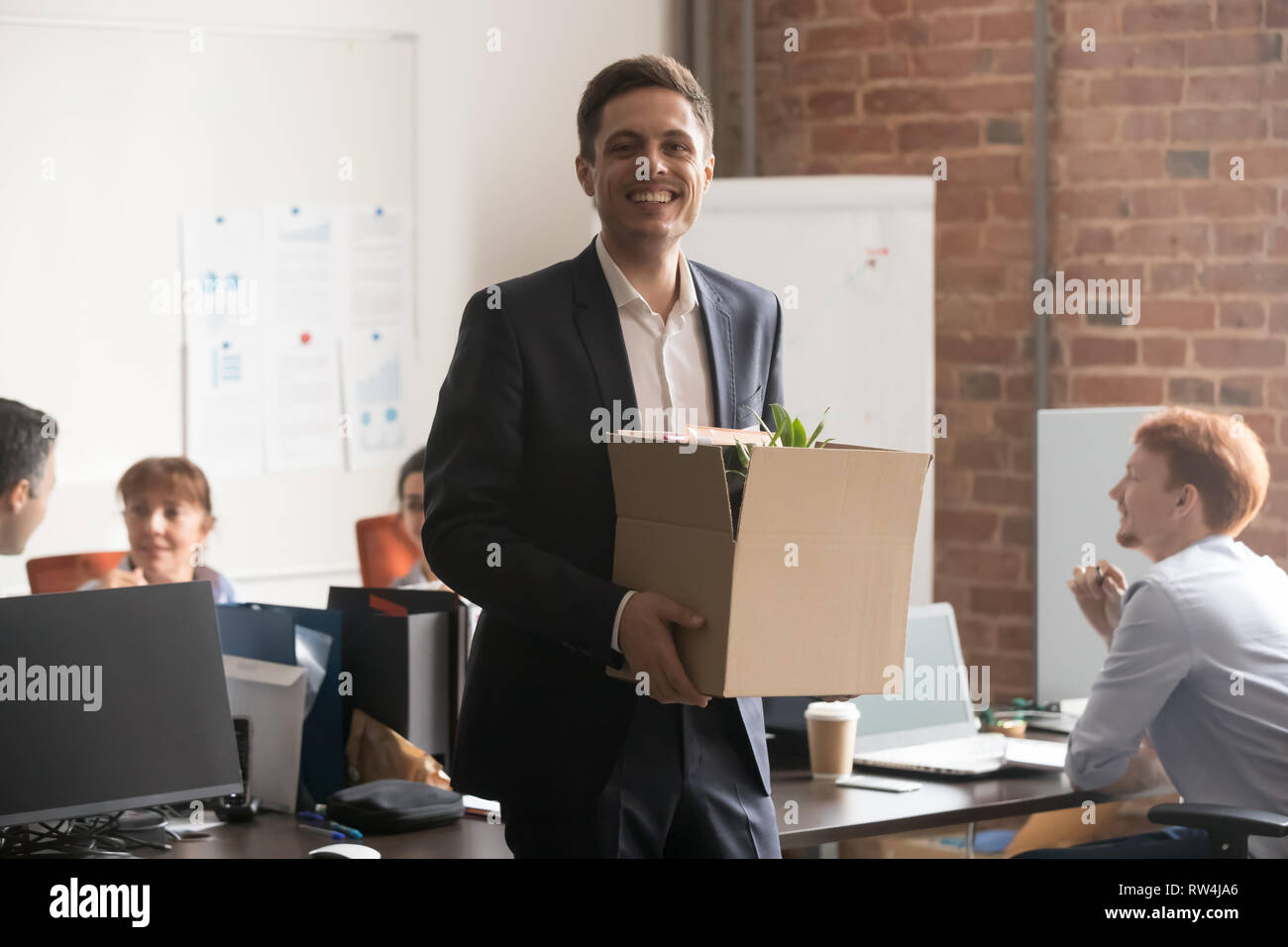 Cheerful male employee holding box with belongings looking at camera ...