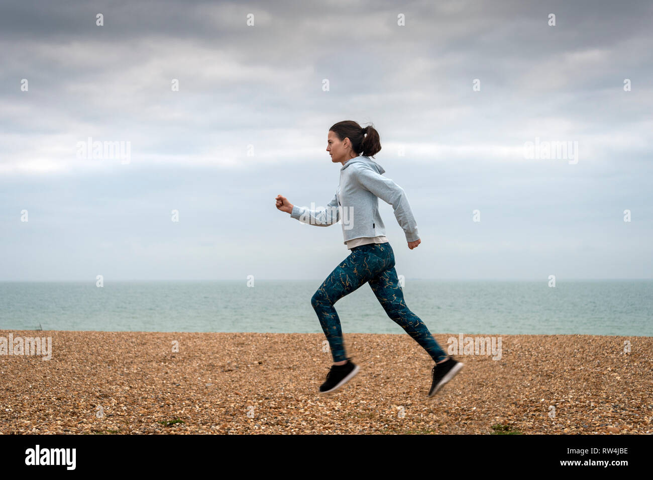woman running along a pebble beach by the sea, keep fit Stock Photo - Alamy