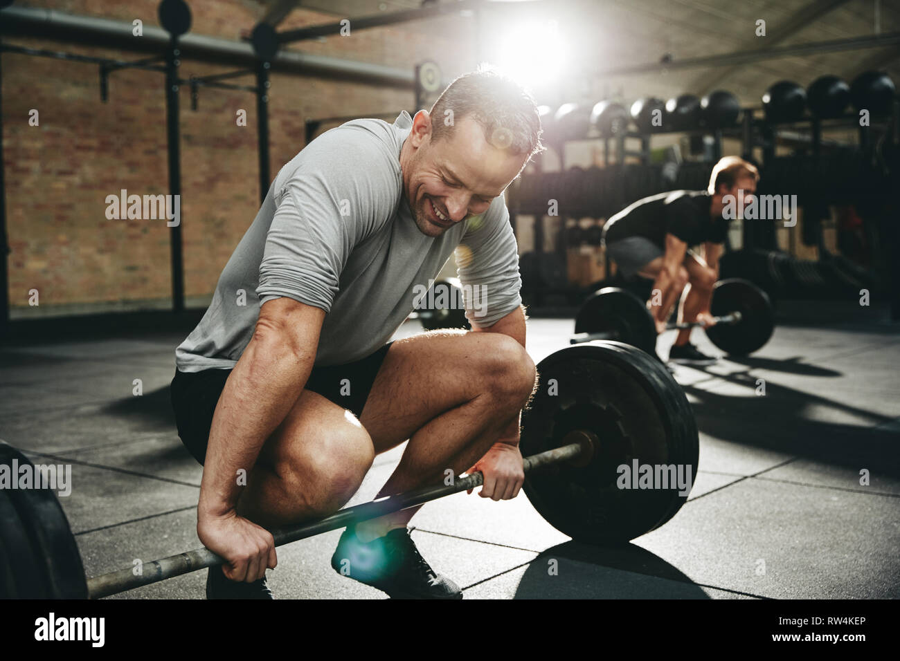Fit man in sportswear laughing while trying to lift a barbell with ...