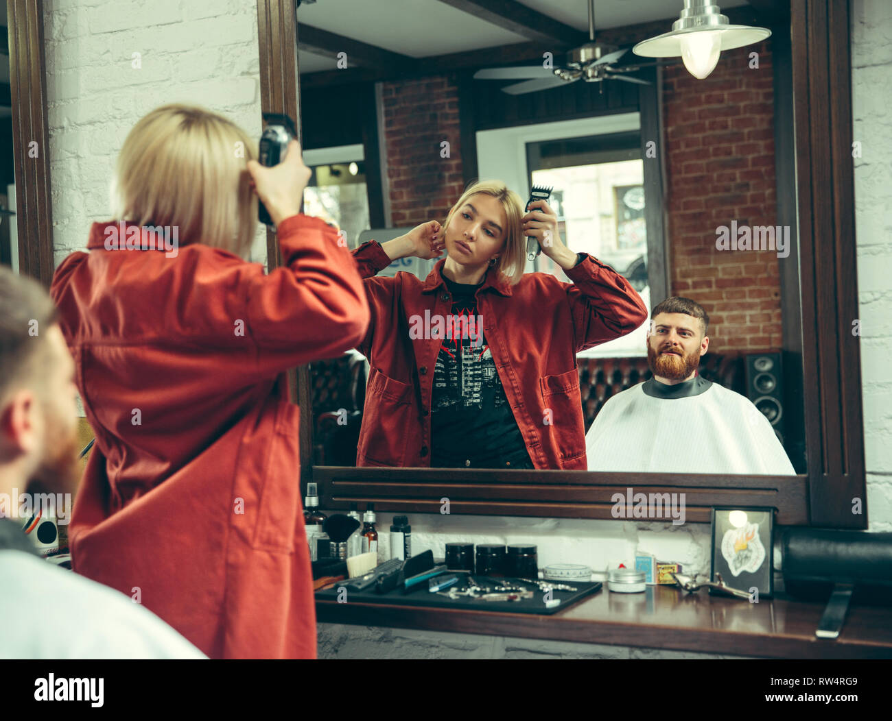Client during beard shaving in barbershop. Female barber at salon ...