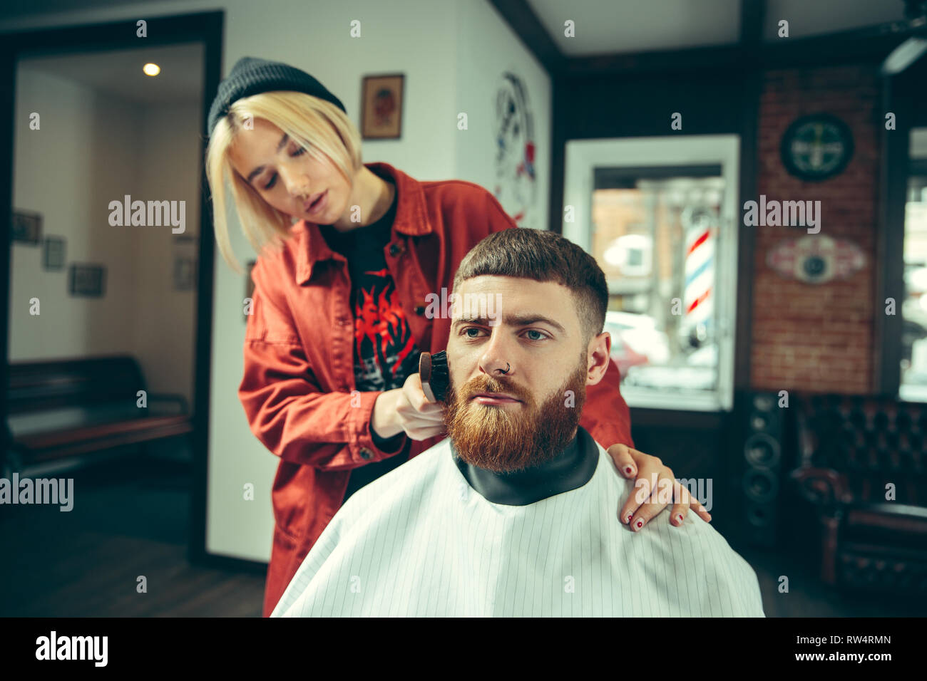Client during beard shaving in barbershop. Female barber at salon ...