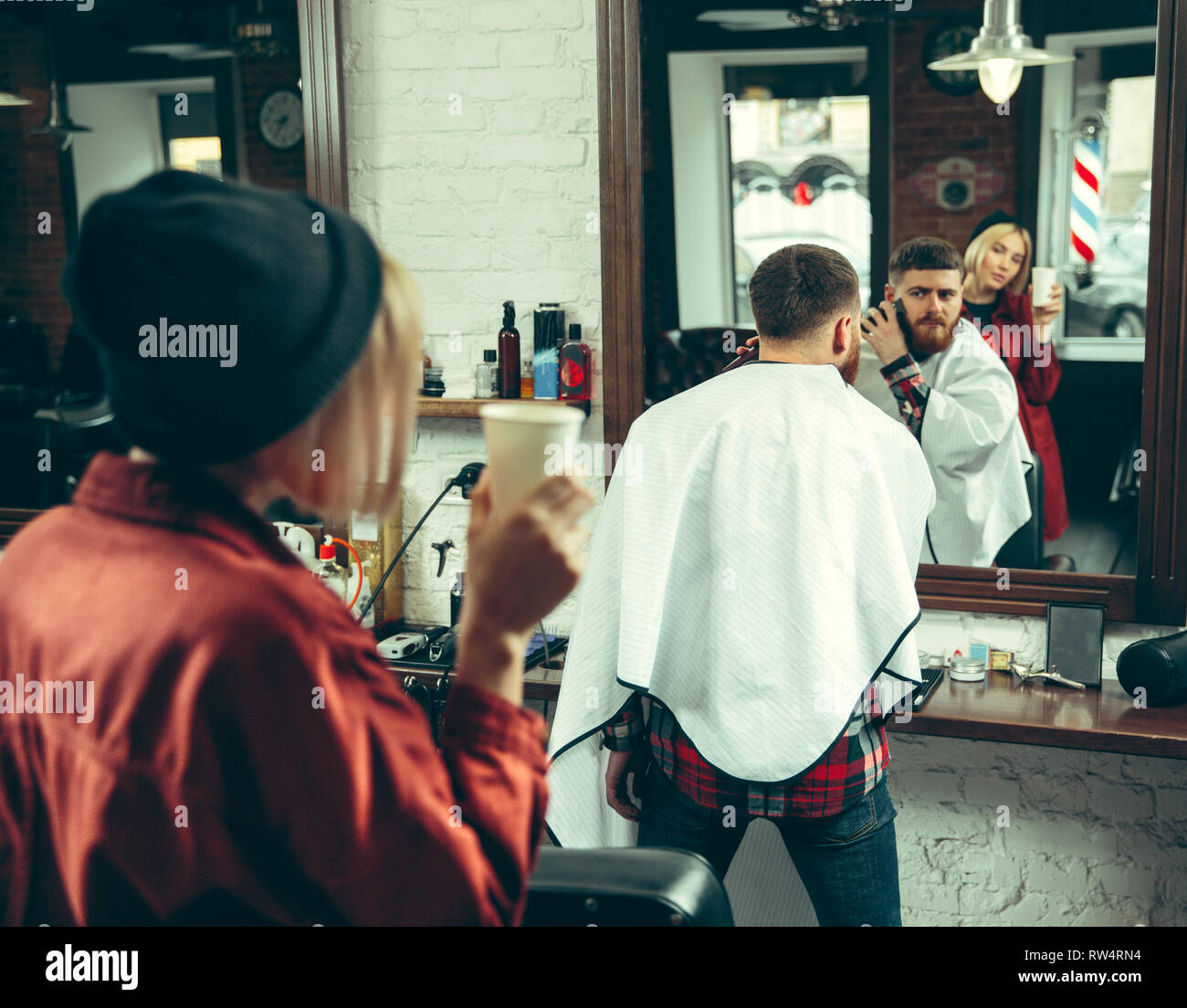 Client during beard shaving in barbershop. Female barber at salon. Gender equality. Woman in the ...