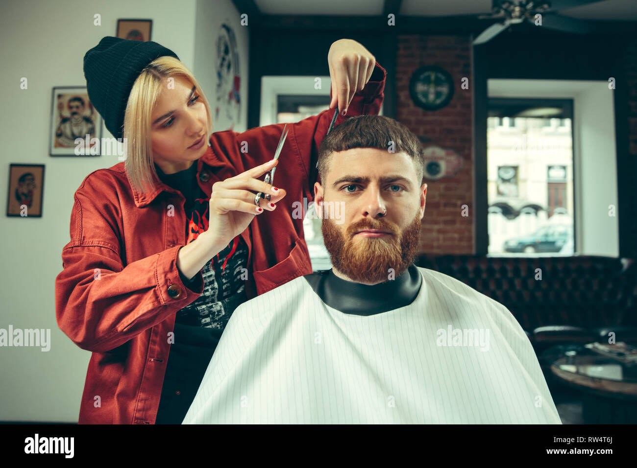 Client during beard shaving in barbershop. Female barber at salon ...