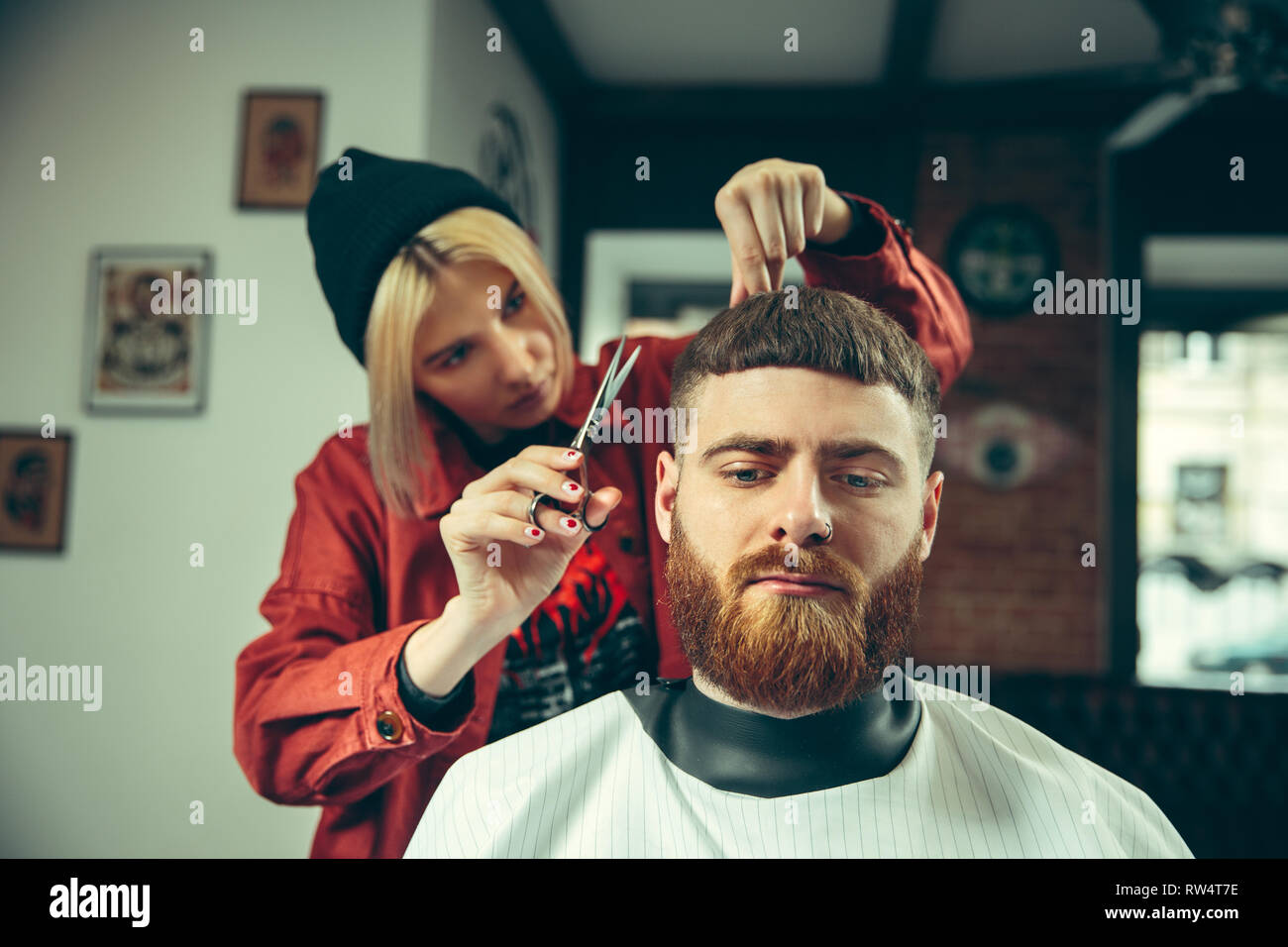 Client during beard shaving in barbershop. Female barber at salon ...