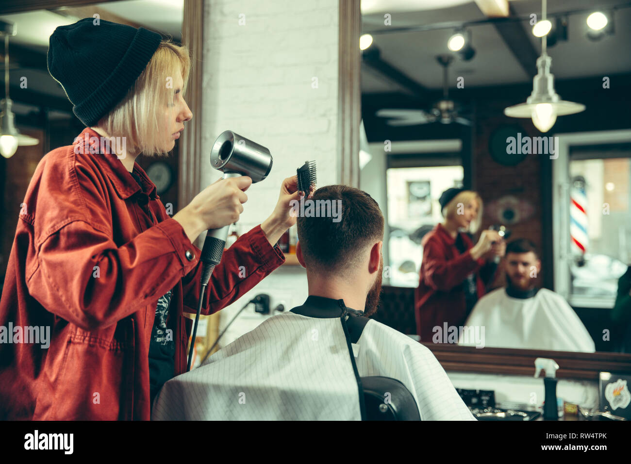 Client during beard shaving in barbershop. Female barber at salon ...