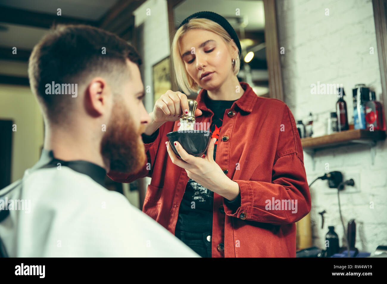 Client during beard shaving in barbershop. Female barber at salon ...