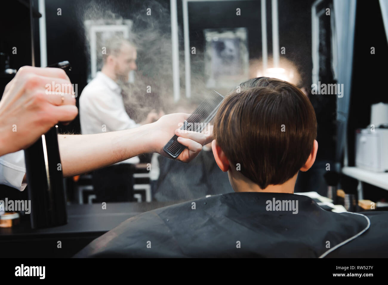 Young handsome barber making haircut of cute boy in barbershop Stock ...