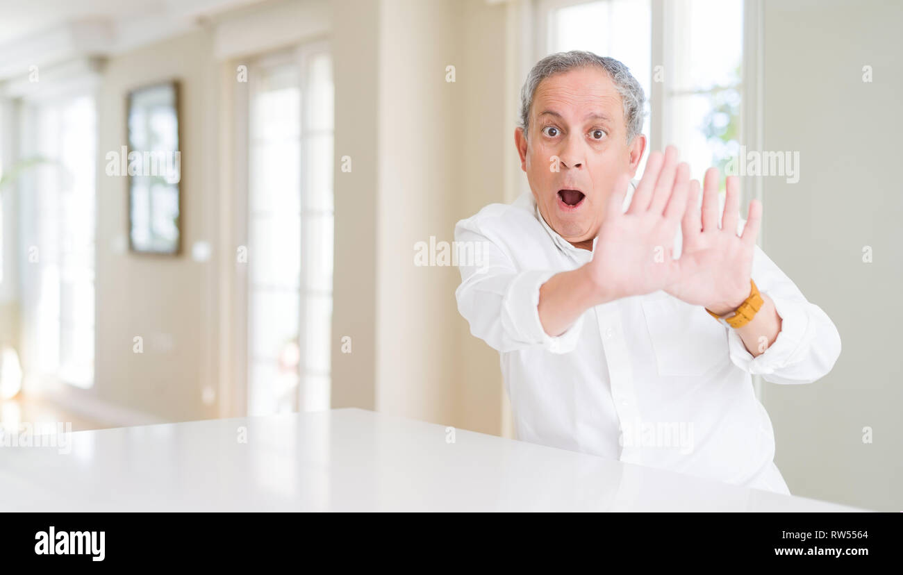Handsome senior man at home afraid and terrified with fear expression ...