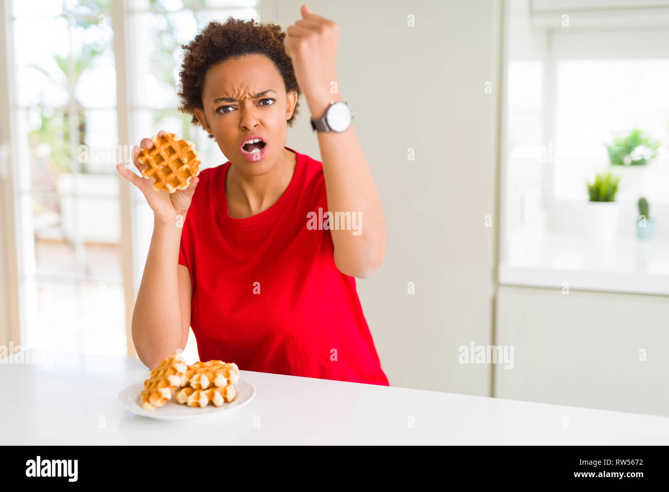 Young african american woman eating sweet waffle annoyed and frustrated ...