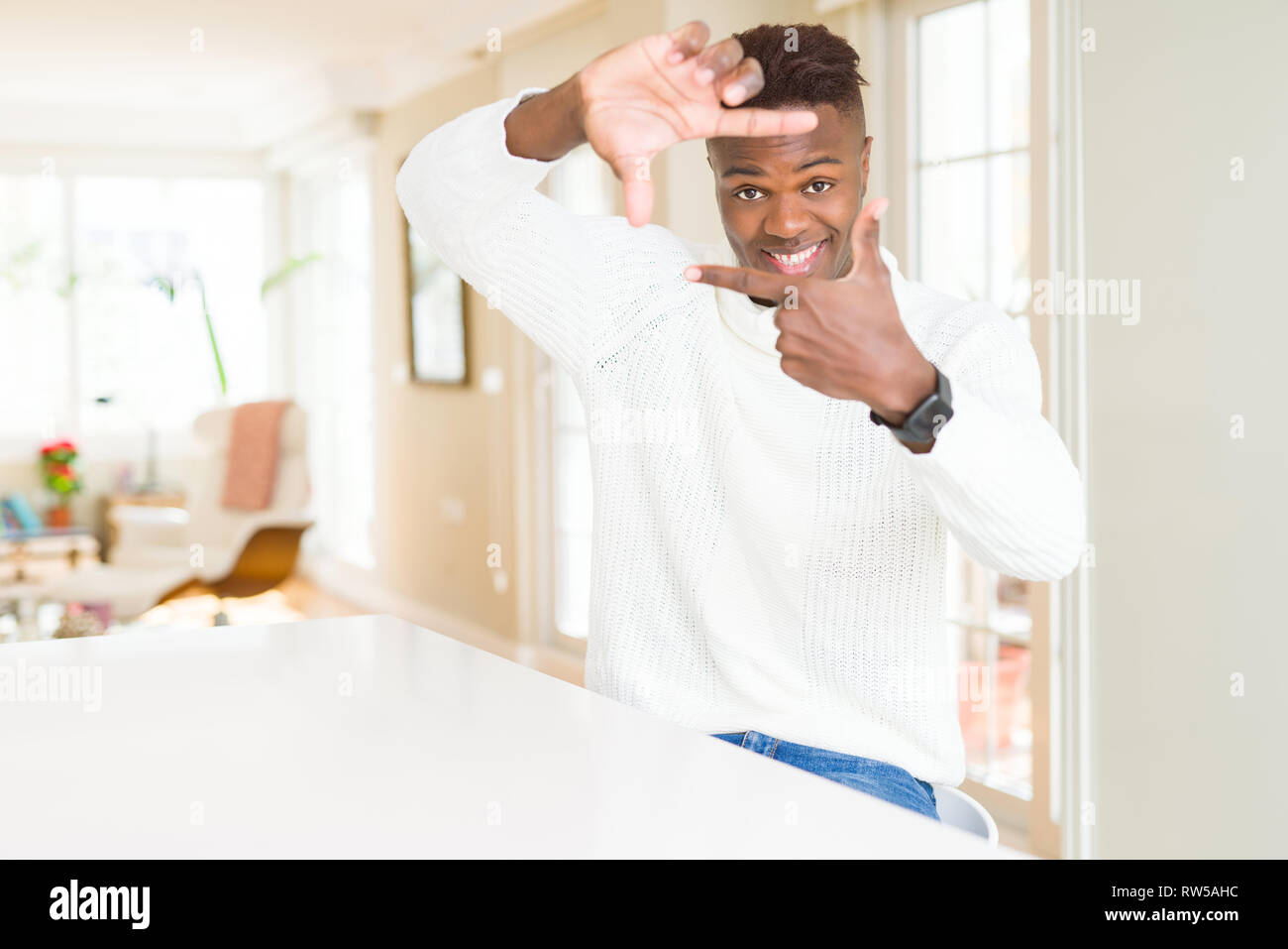 Handsome african american man on white table smiling making frame with ...