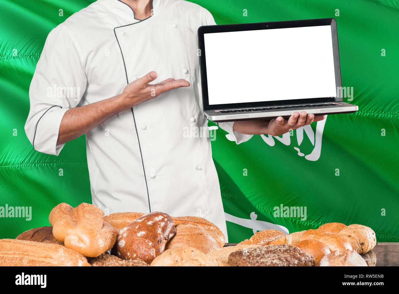 Saudi Baker holding laptop on Saudi Arabia flag and breads background ...