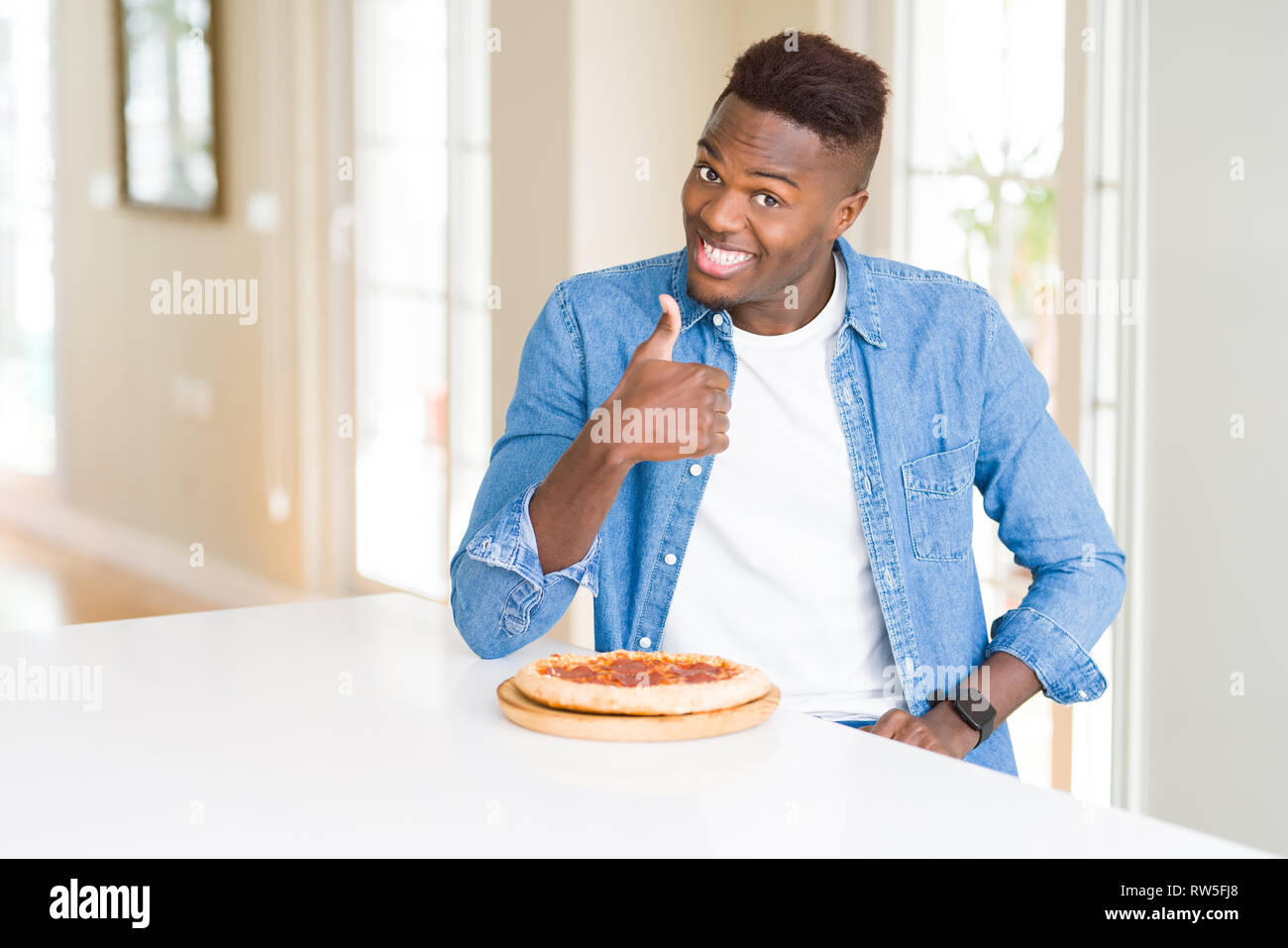 African american man eating pepperoni pizza at home happy with big ...