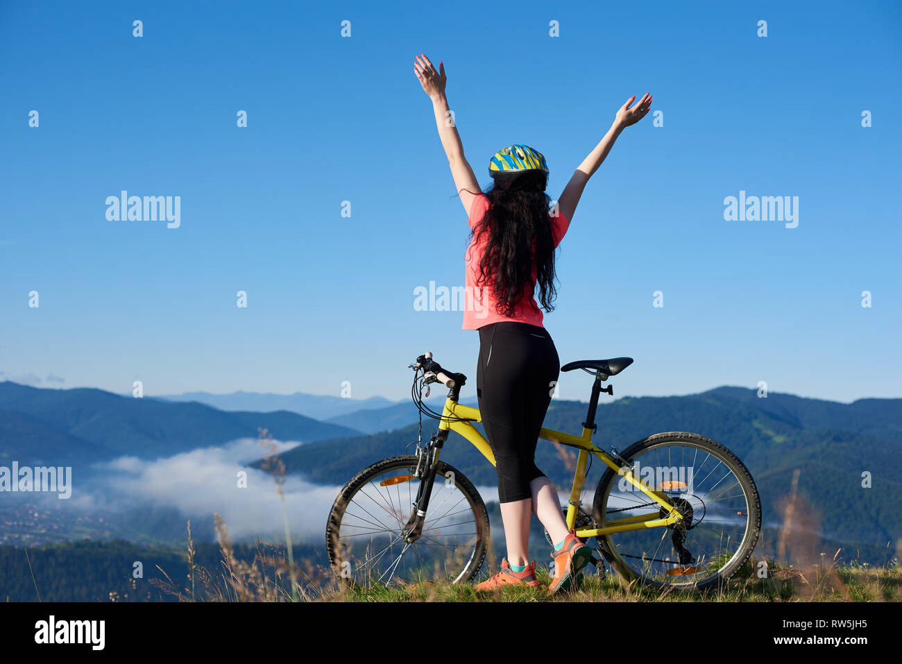 Back view of sporty female biker standing with her hands up with yellow ...