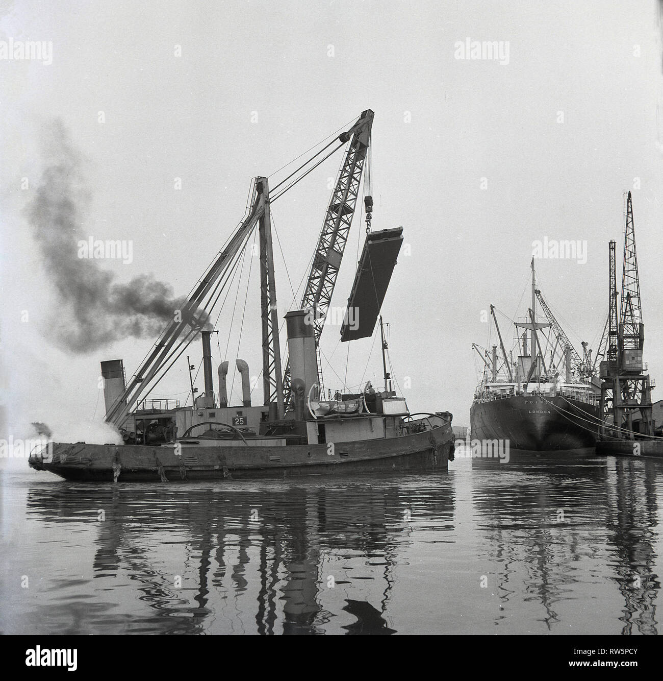 1950s, London docks, England, a steam-powered tugboat beside a platform ...