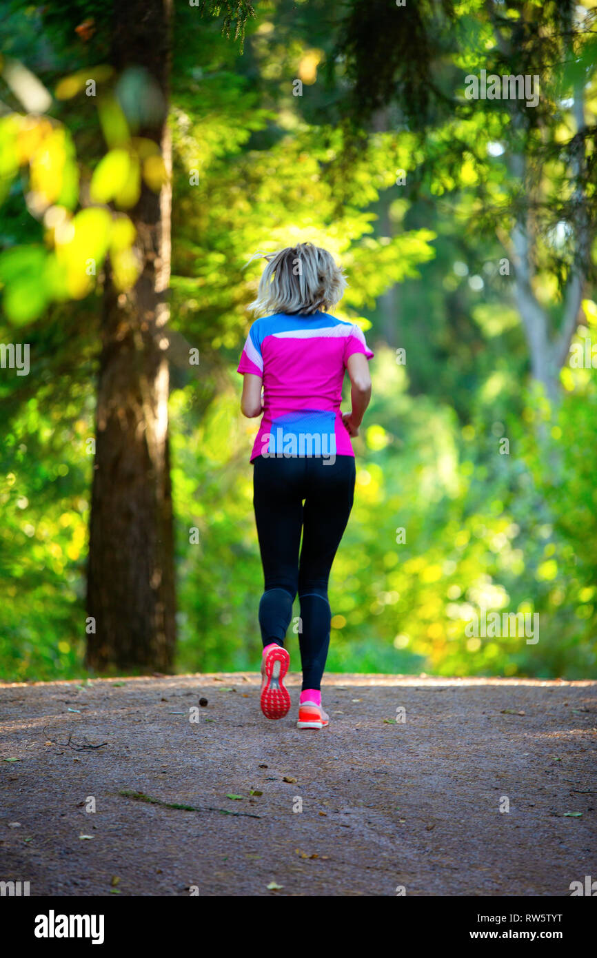 Photo from back of blonde athlete woman running through park among ...