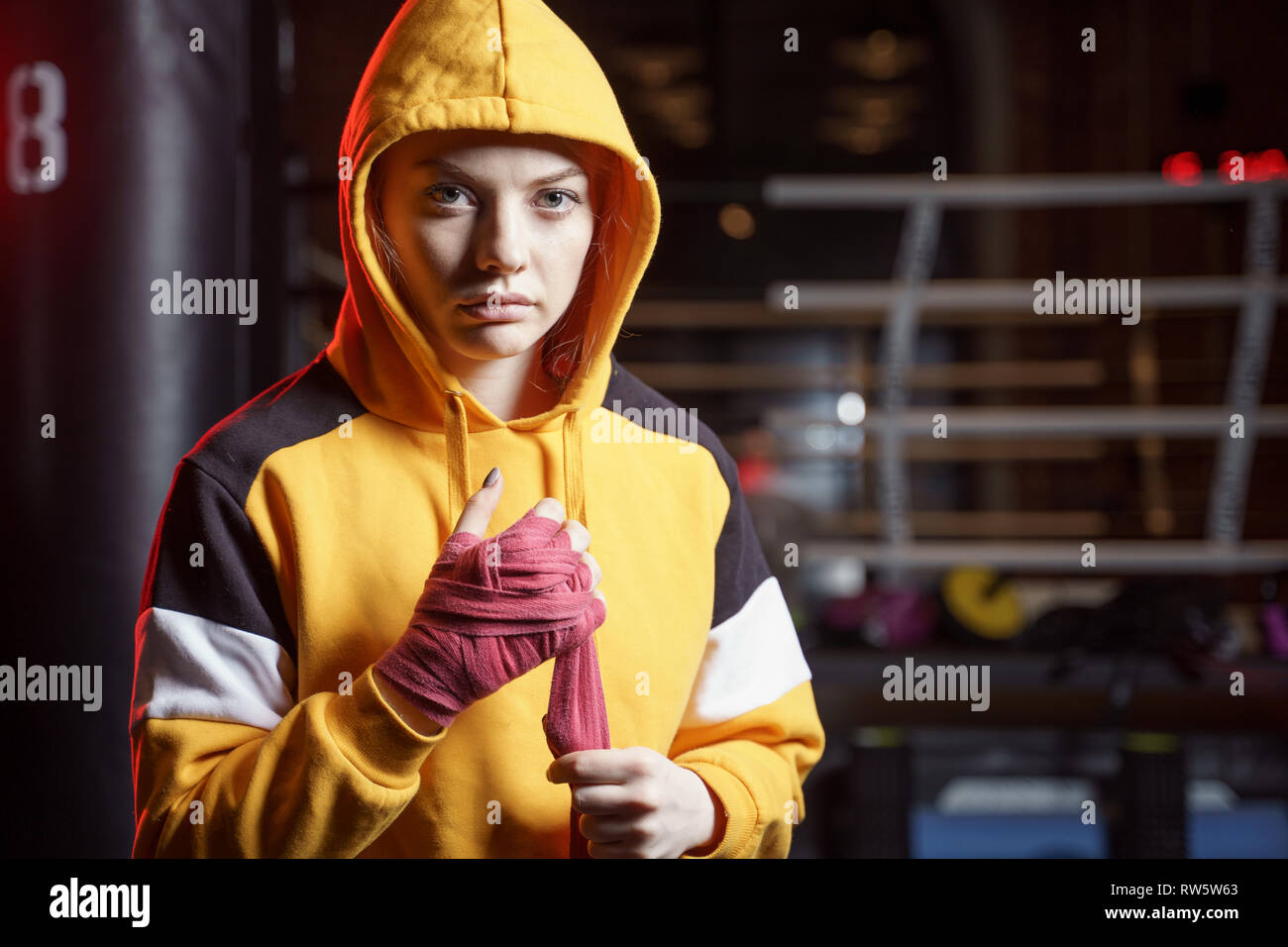 Female boxer pulls red bandages around her hands on ring against black ...