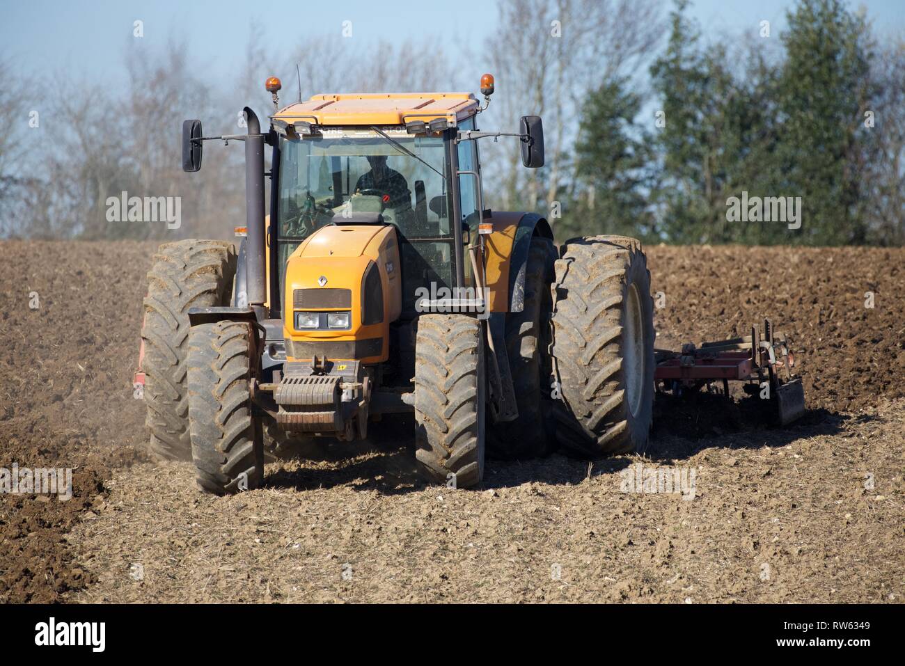 A French farmer operating a tractor with dual wheels and a spring tine ...