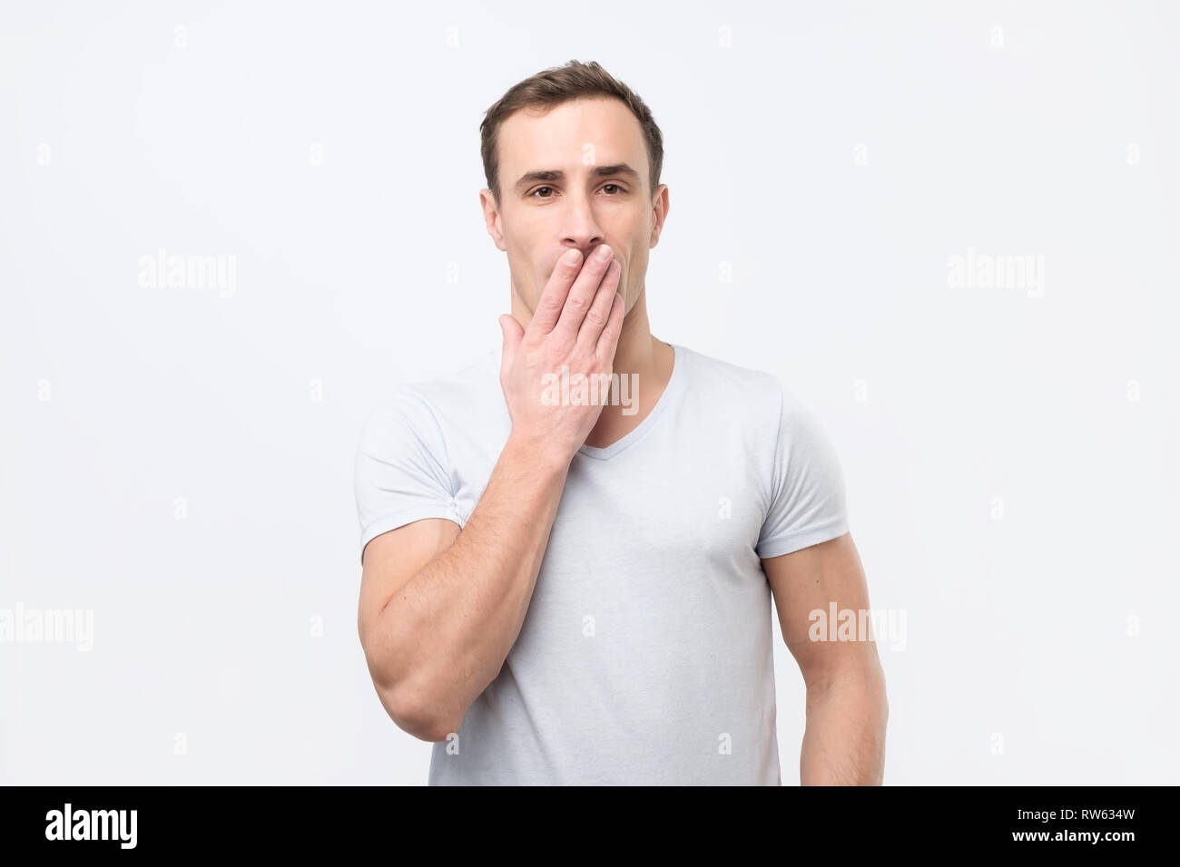 Shocked young italian man in white t-shirt covering mouth with hands ...