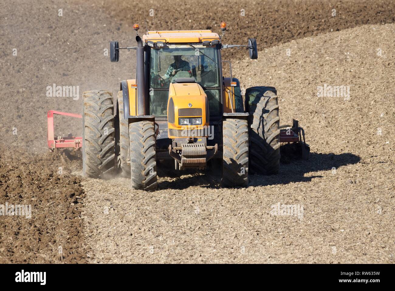 A French farmer operating a tractor with dual wheels and a spring tine ...