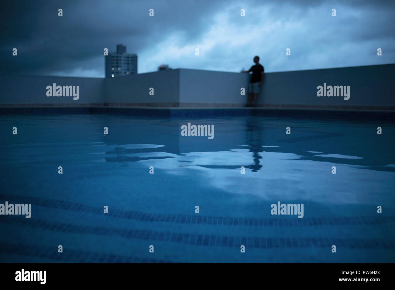 Man standing alone by a swimming pool on a rooftop of a luxury ...