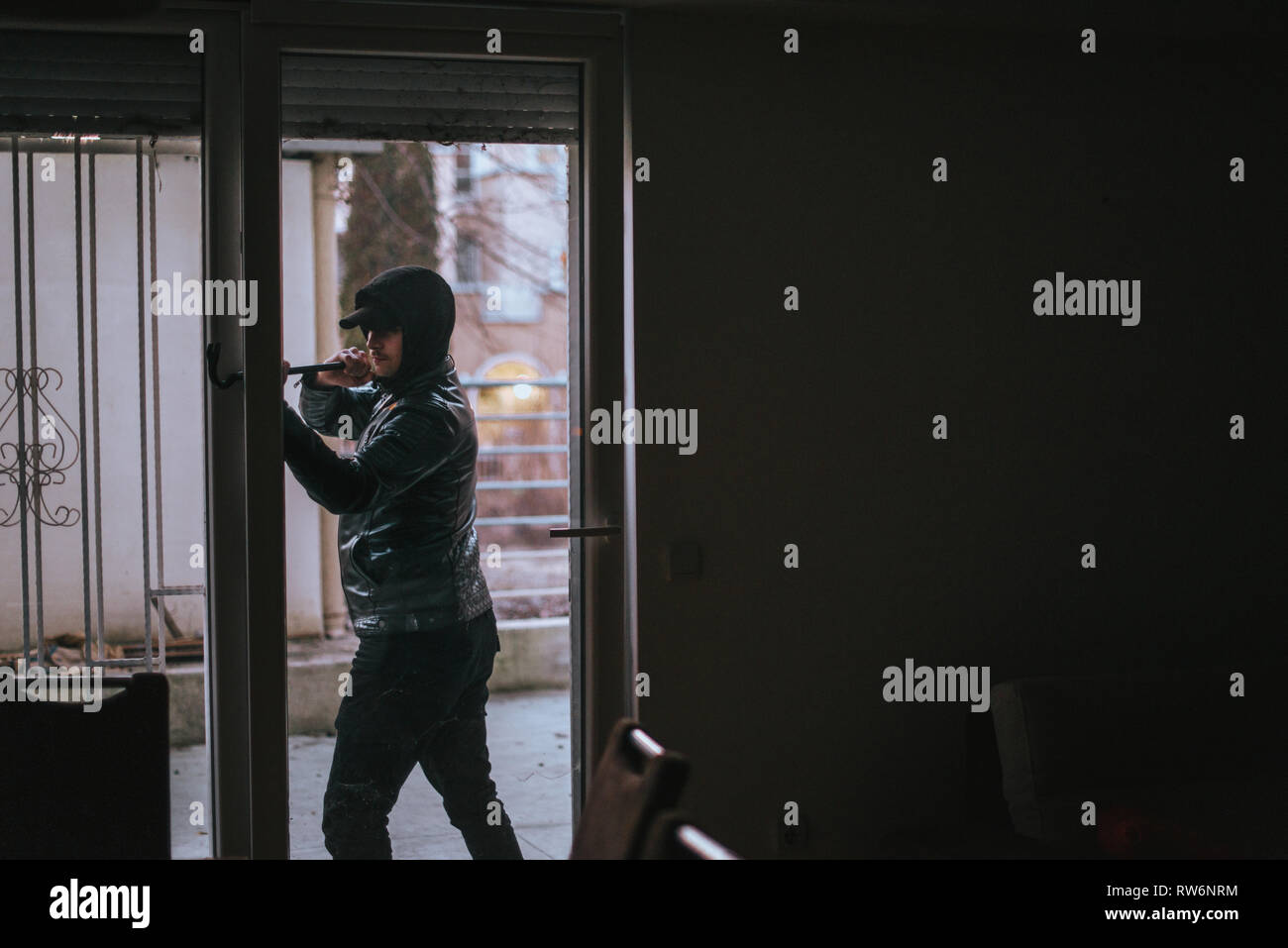 Hooded man using wrecking bar to open glass door Stock Photo - Alamy