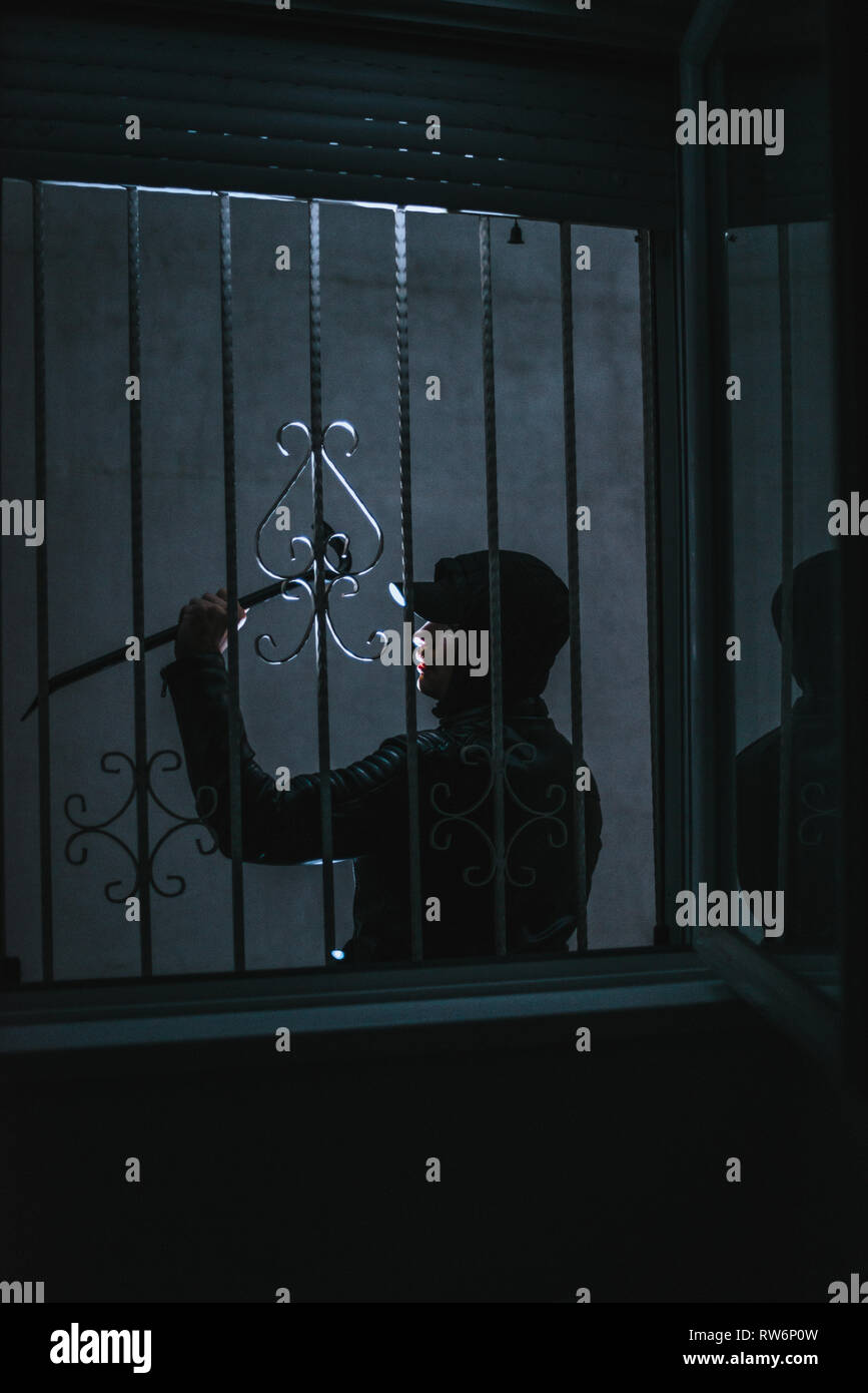 Hooded man using wrecking bar to open window Stock Photo - Alamy